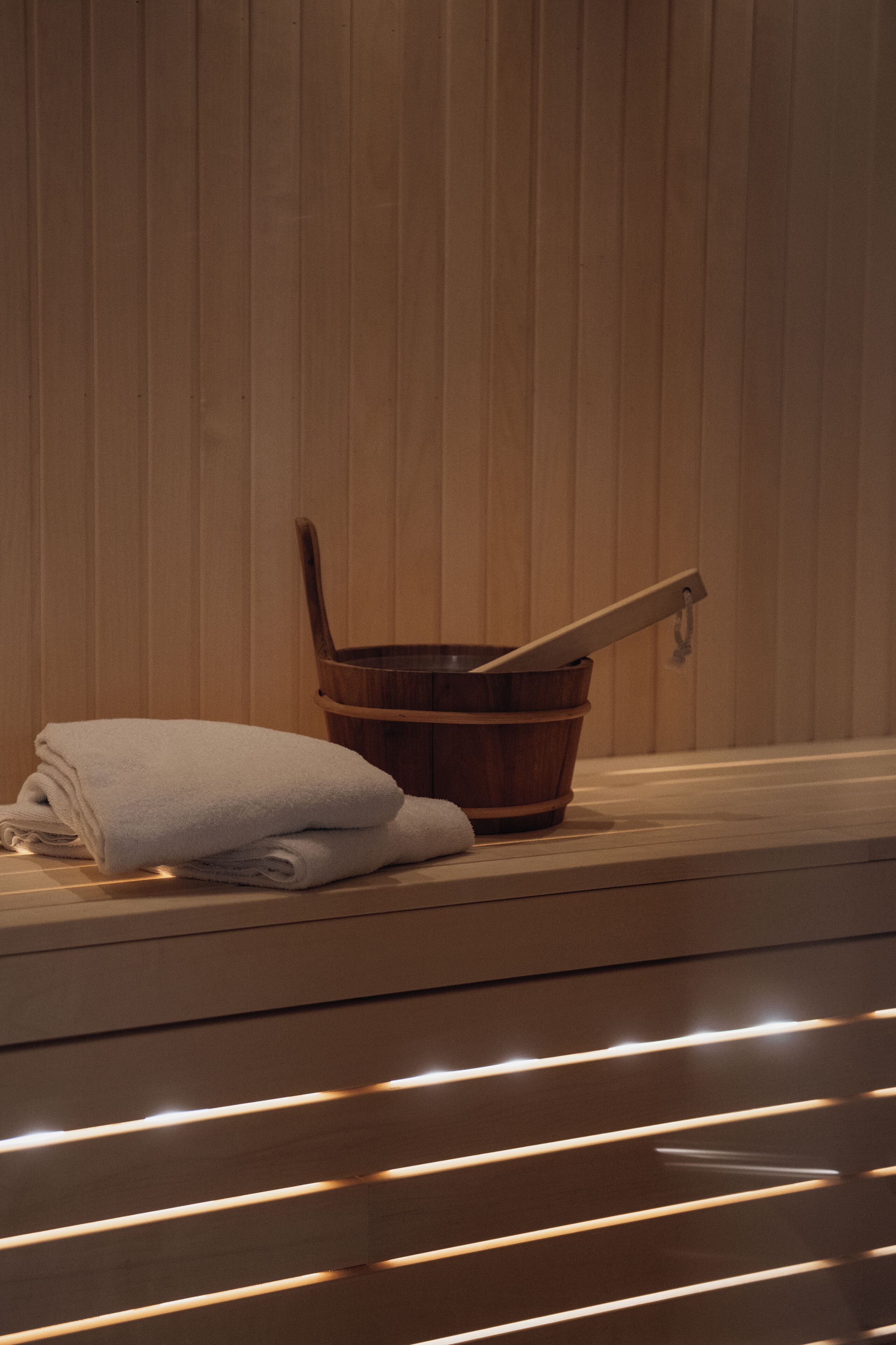 Banco de sauna de madeira com uma toalha e um balde de madeira.