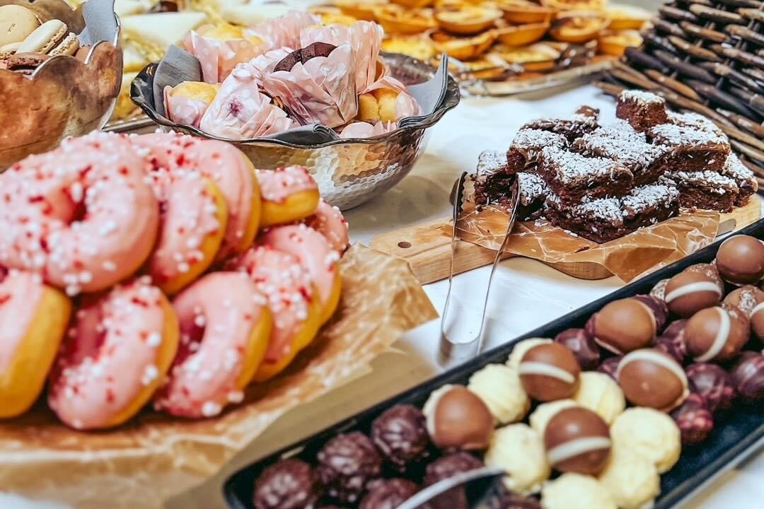 Diversos doces e sobremesas sobre uma mesa, incluindo donuts, biscoitos e guloseimas cobertas de chocolate.