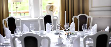 Mesa de jantar formal posta com toalhas brancas, cadeiras e louça fina.