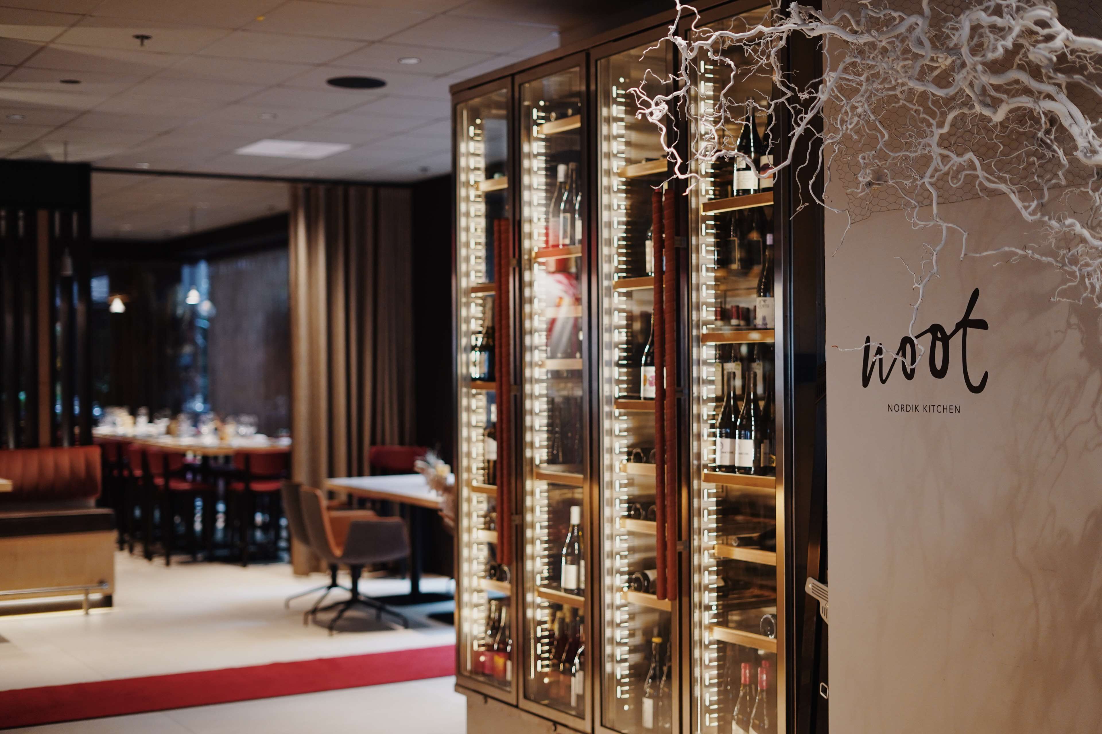 Interior de restaurante com design moderno, apresentando uma vitrine de vidro com garrafas e uma placa com a inscrição 'Nordik Kitchen'.