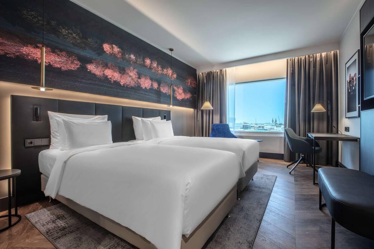 Quarto de hotel com uma cama grande, uma escrivaninha, uma cadeira e vista para a cidade.