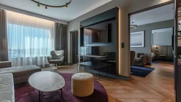 Uma sala de estar moderna com sofá, pufê e mesa de centro, uma televisão de tela plana na parede e uma área de jantar com mesa e cadeiras de vidro.
