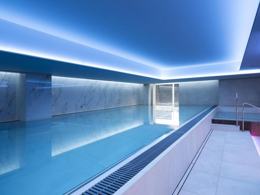 Piscina interior moderna com design elegante, paredes de mármore e barreira de vidro.
