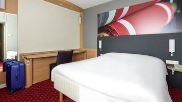 Quarto de hotel com uma cama, uma escrivaninha, uma cadeira, telefone e luminária na parede.