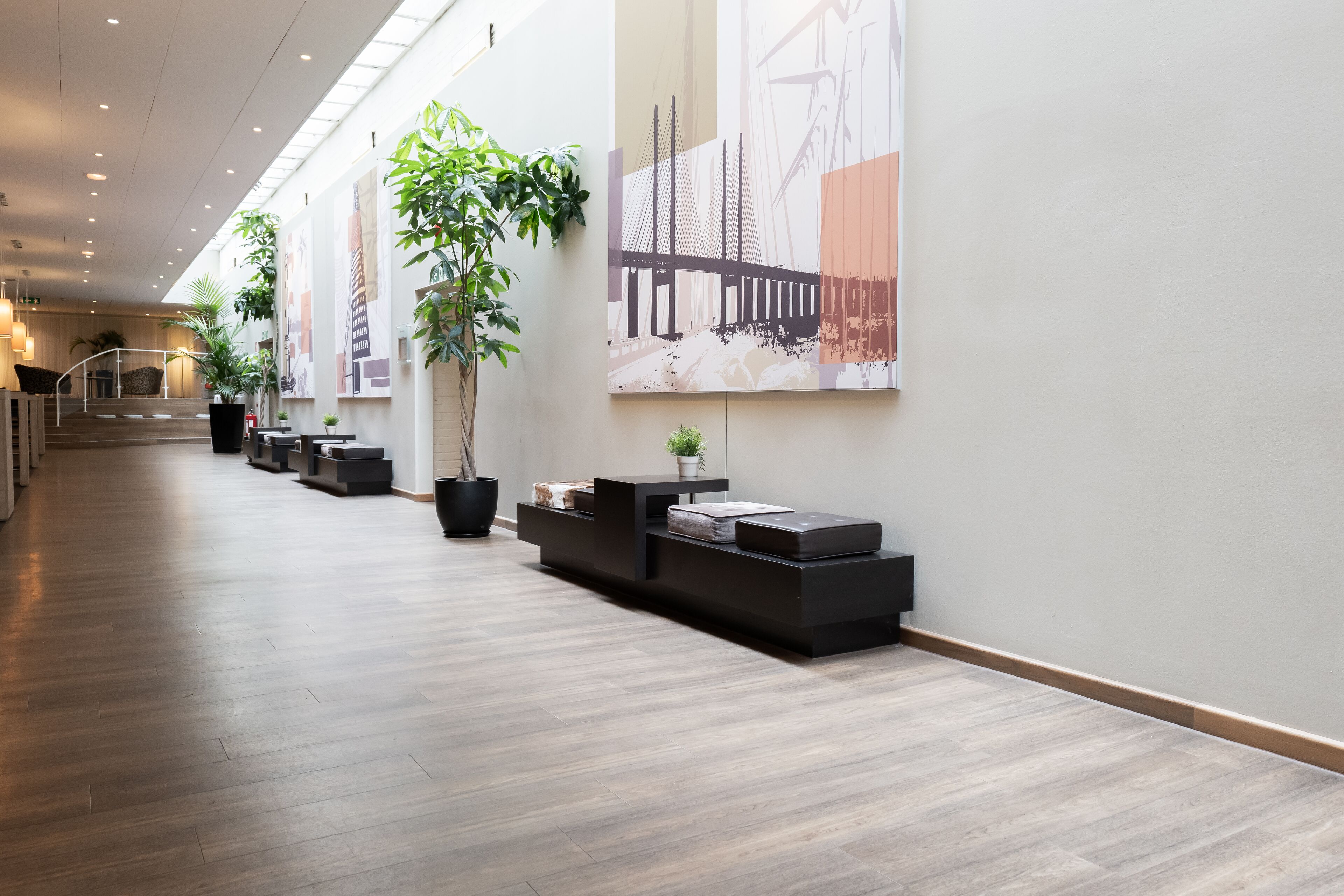 Um lobby de hotel moderno com um balcão de recepção extenso, plantas em vasos e grandes obras de arte nas paredes.