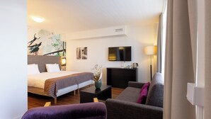 Quarto de hotel com cama, sofá, televisão e uma pequena mesa com um vaso.