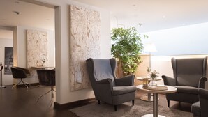 Uma sala de estar moderna com uma poltrona cinza, uma mesa de centro redonda e uma grande planta em vaso.