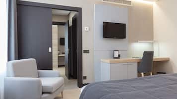 Quarto de hotel com cama, escrivaninha, cadeira, televisão e poltrona estampada.