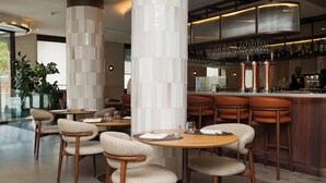 Restaurante moderno com mesas redondas e cadeiras acolchoadas, área de bar com torneiras de cobre e uma grande estrutura de pilar.