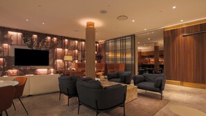 Um hall de hotel moderno com televisão de tela plana, assentos confortáveis, uma mesa de centro e um bar ao fundo.