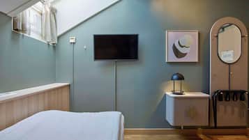 Quarto com cama, televisão, mesa de cabeceira, espelho e janela com cortinas.
