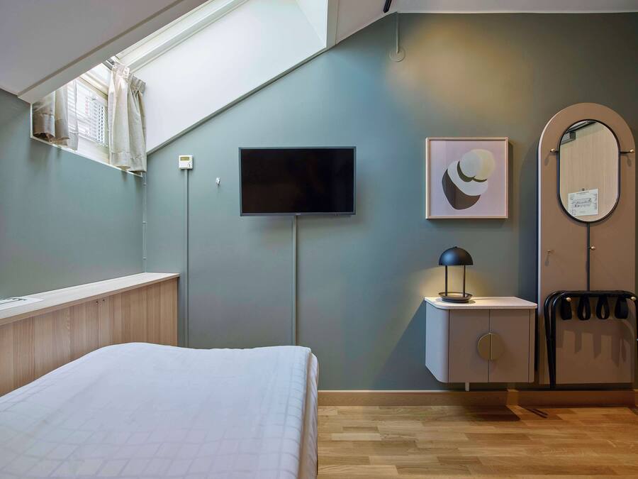 Quarto com cama, televisão, mesa de cabeceira, espelho e janela com cortinas.