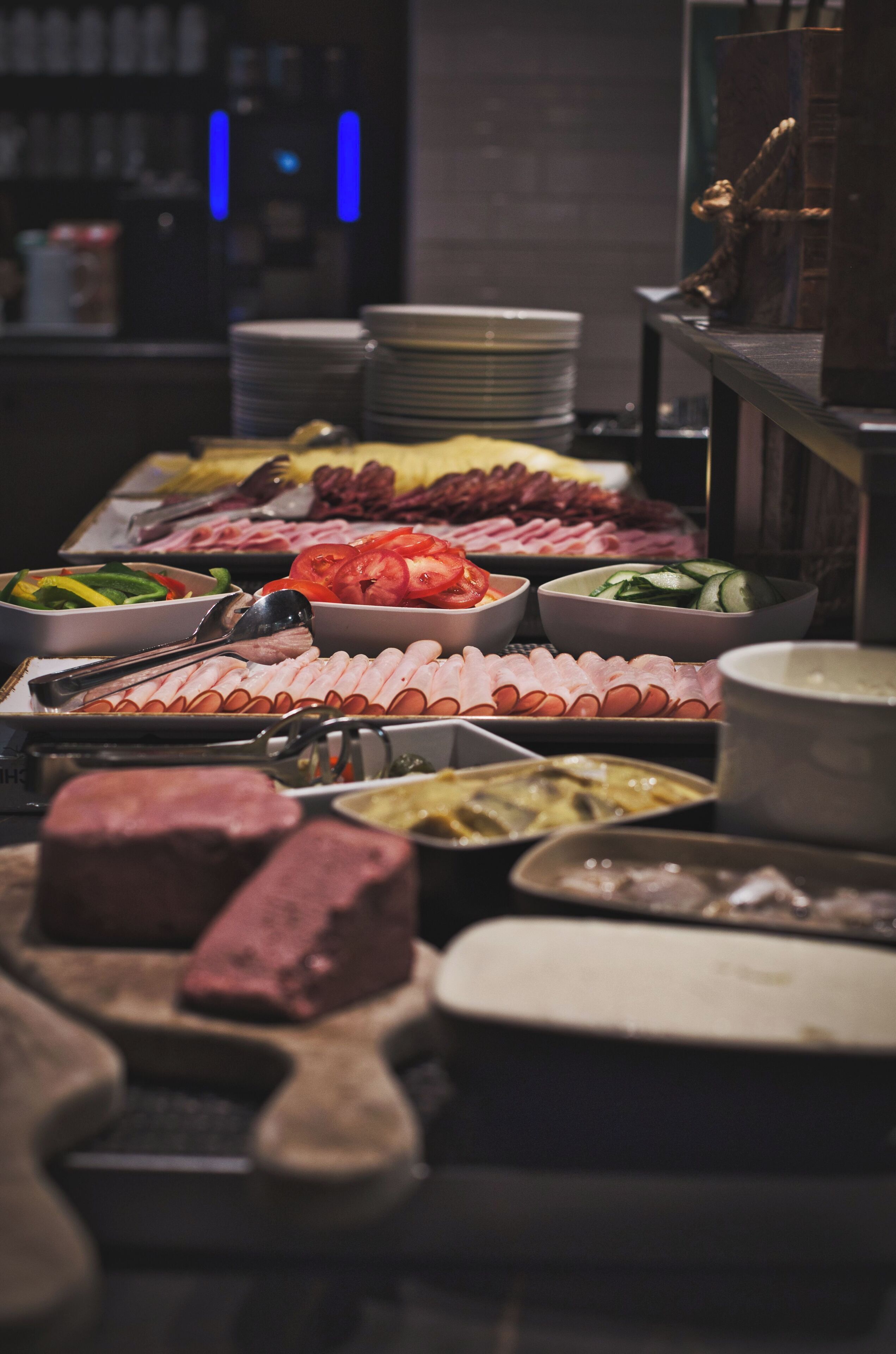 Buffet com diversos alimentos, incluindo carnes fatiadas, legumes e queijos.