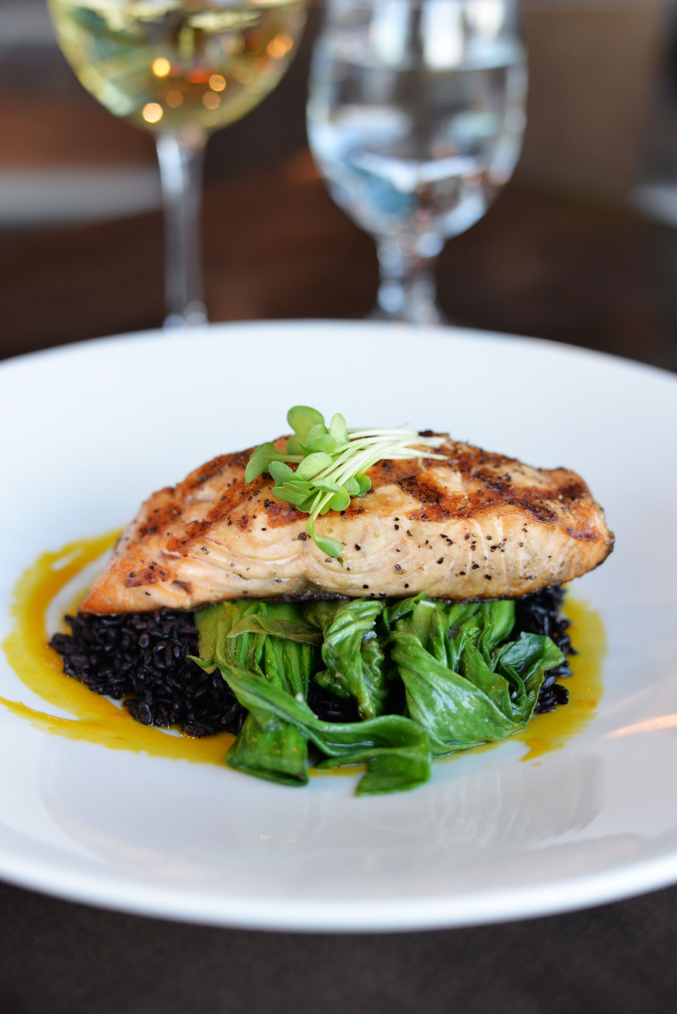 Um prato com um pedaço de peixe grelhado, legumes verdes e risoto preto.