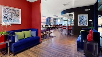 Um hall de hotel moderno com sofá azul, paredes vermelhas e piso de madeira.