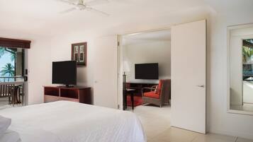 Quarto de hotel com cama, escrivaninha com televisão, uma cadeira e porta que dá para outro cômodo.