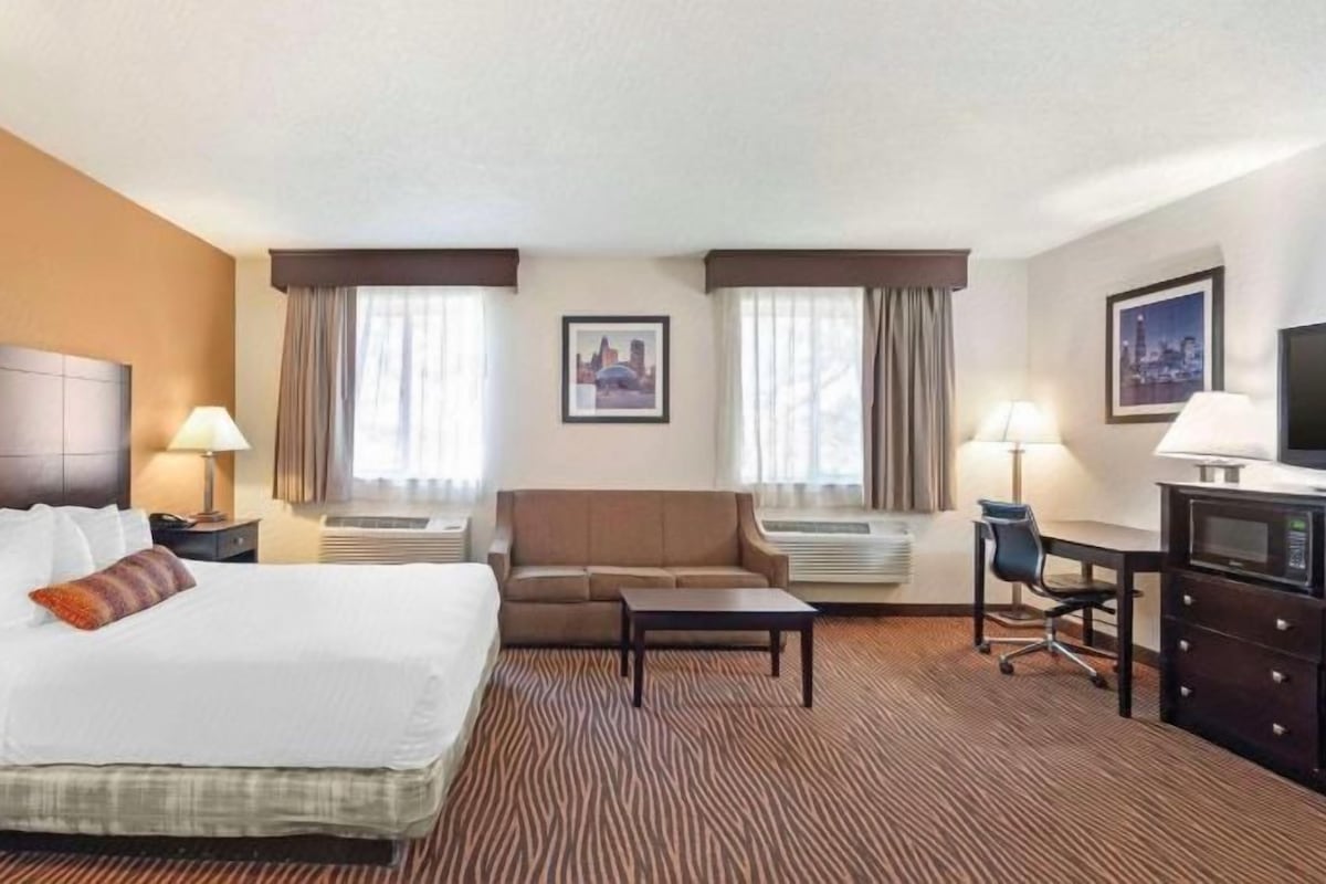 Quarto de hotel com cama, escrivaninha, cadeira, sofá e televisão.