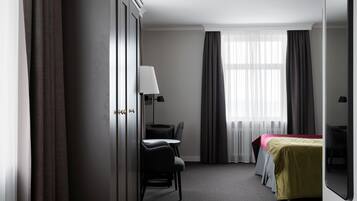 Quarto de hotel com cama, escrivaninha, cadeira, luminária e guarda-roupa.