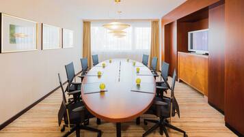 Uma sala de conferências com uma grande mesa oval, cadeiras, uma televisão e quadros nas paredes.