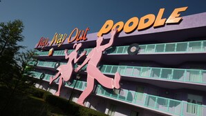 Um hotel com uma placa que diz 'Way Out Poodle' e uma grande escultura rosa de uma pessoa.