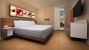 Quarto de hotel com uma cama grande, uma mesa de cabeceira, um armário e uma televisão de tela plana, além de uma obra de arte com o tema do Mickey Mouse na parede.