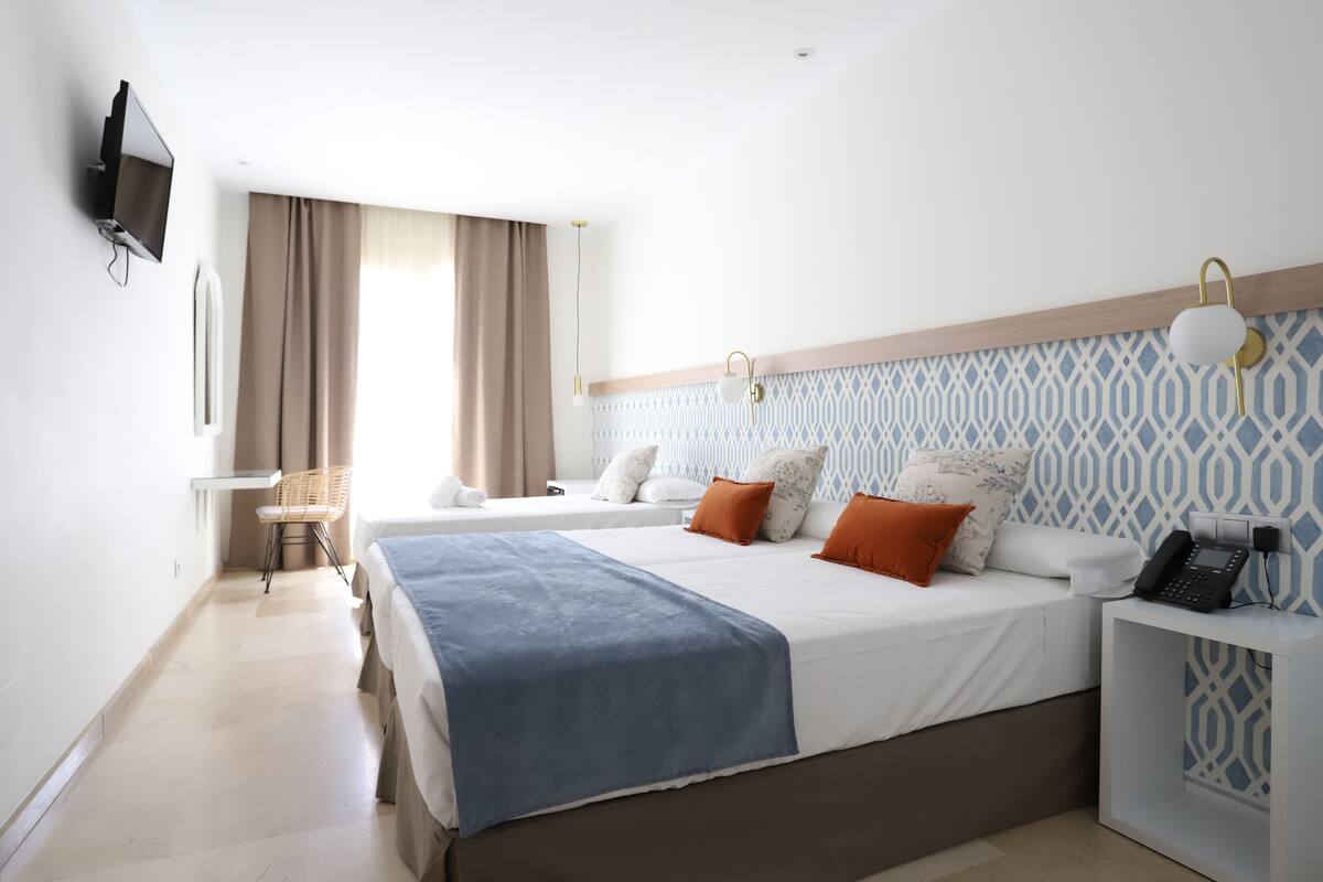 Quarto de hotel com cama, mesa de cabeceira com telefone, televisão na parede e parede estampada.