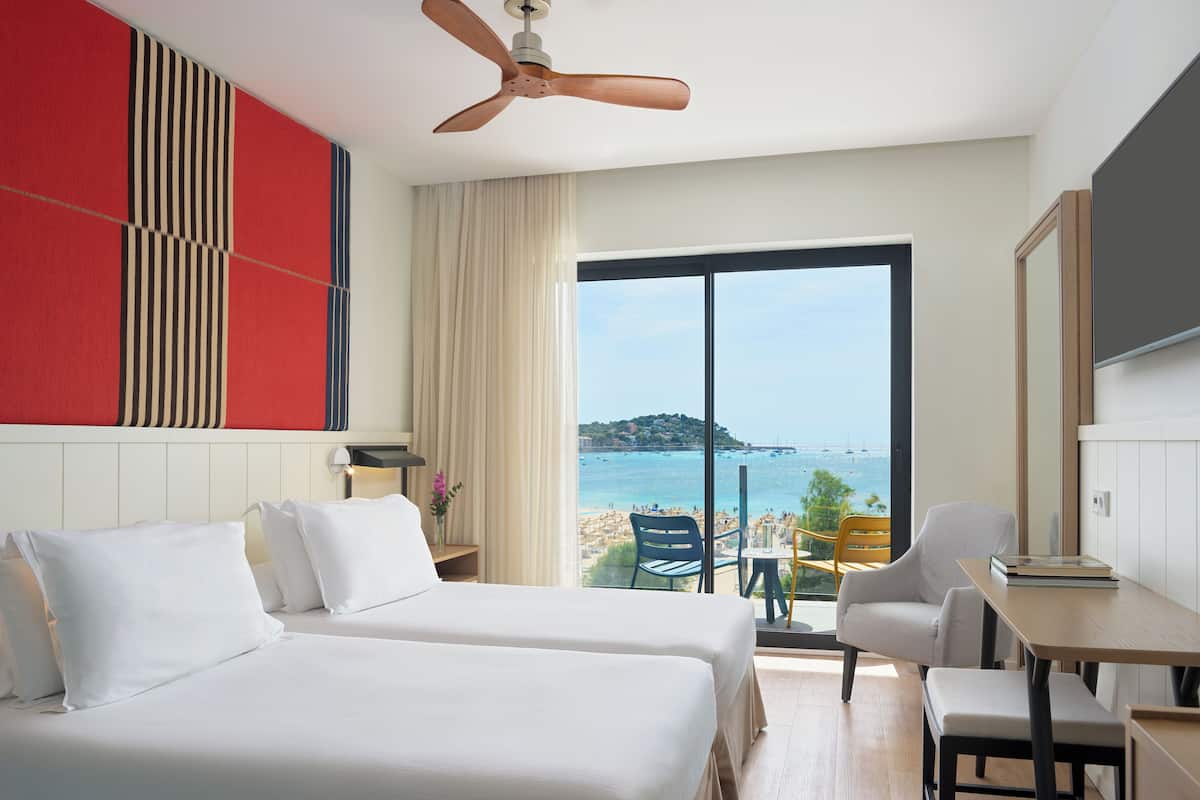 Quarto de hotel com duas camas, uma escrivaninha e vista para o mar.