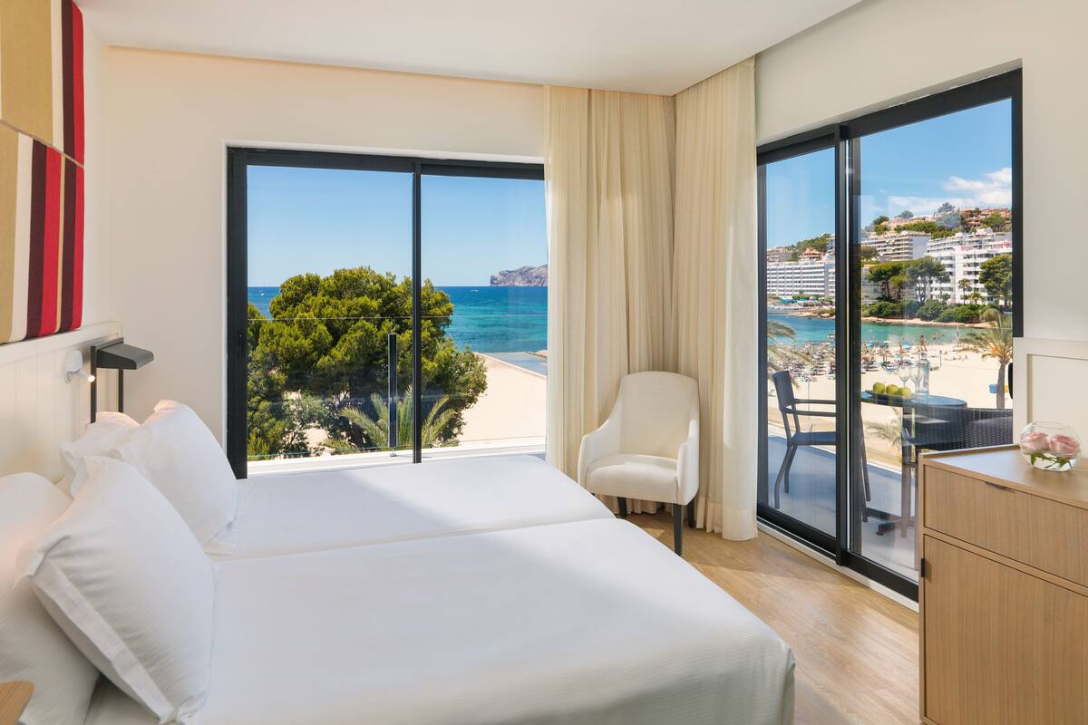 Quarto de hotel com uma cama grande, uma cadeira, uma escrivaninha e vista para a praia e o oceano.