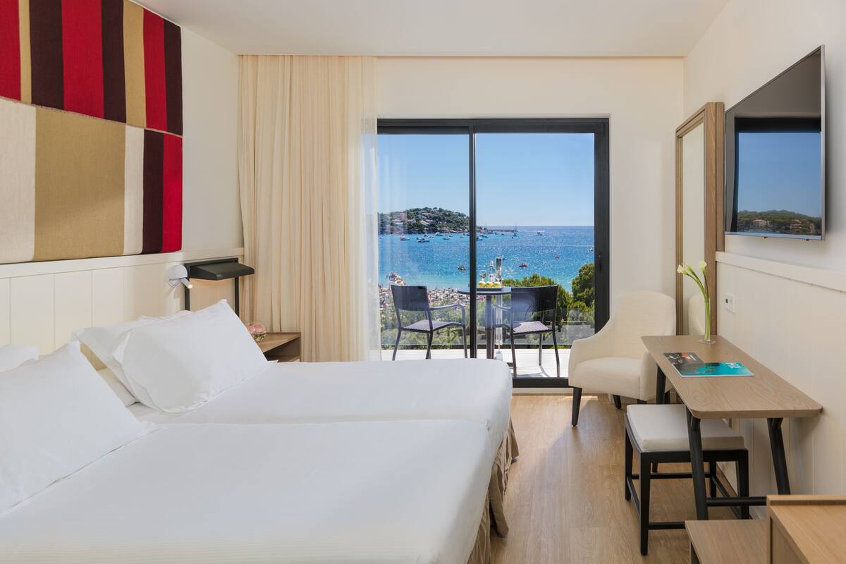Quarto de hotel com uma cama grande, uma escrivaninha e vista para o mar.