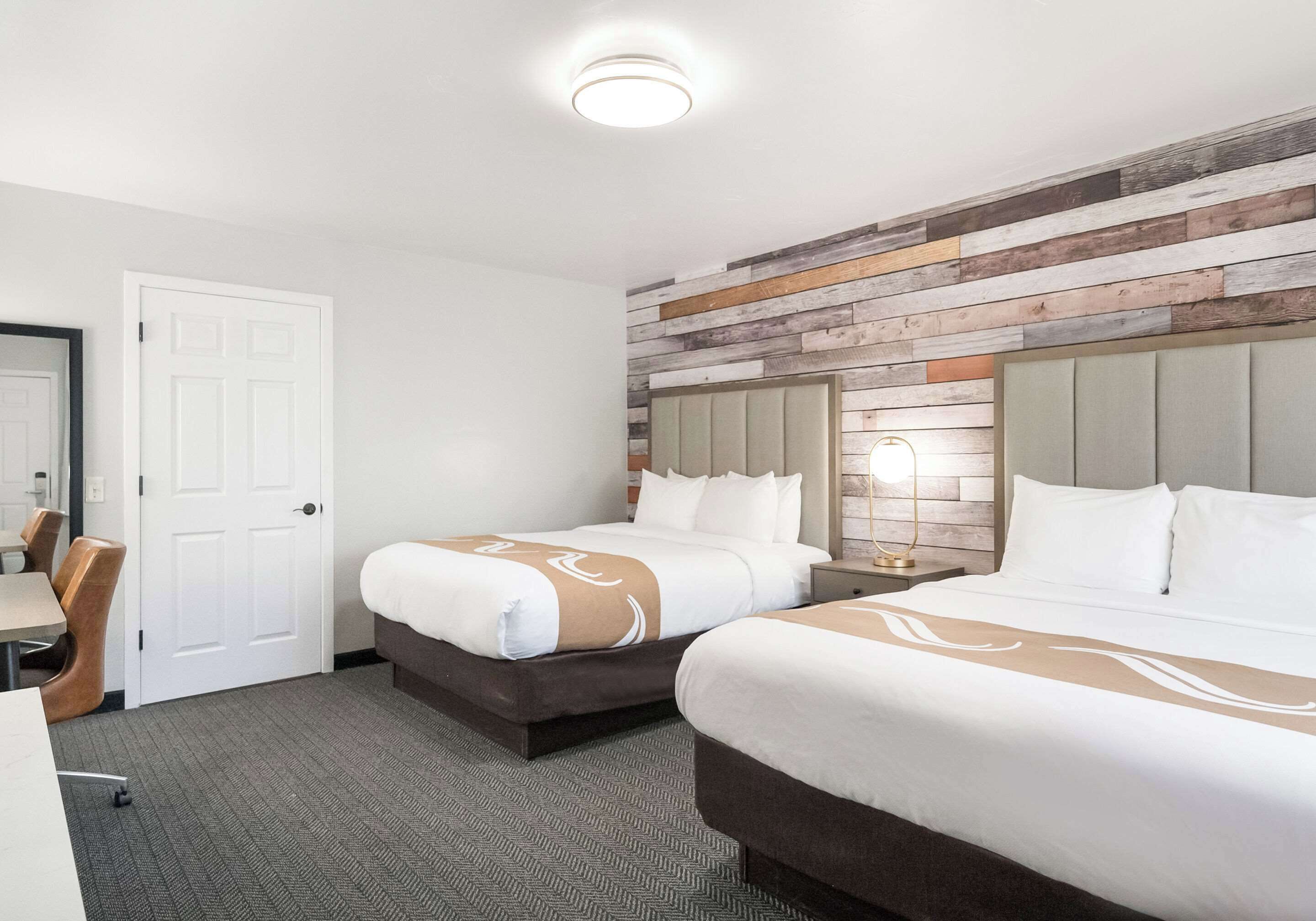 Quarto de hotel com duas camas, uma mesa e uma cadeira.