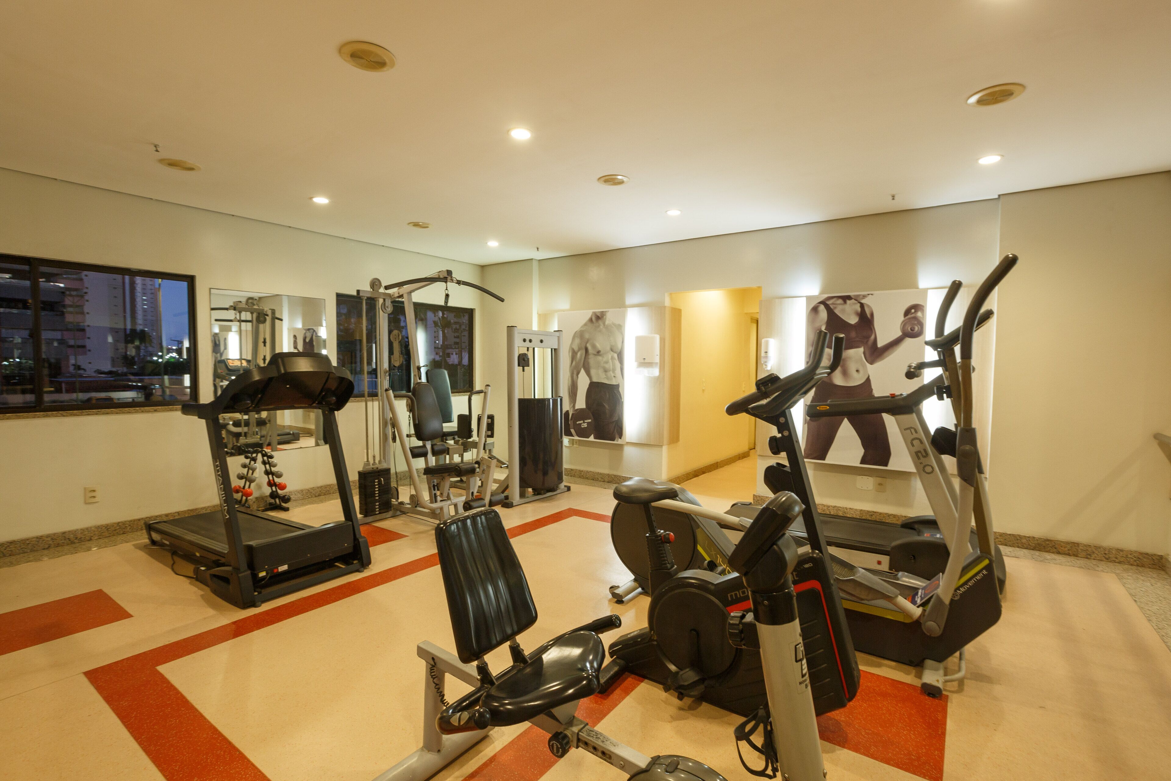Uma academia com equipamentos de cardio, aparelhos de musculação e um espelho refletindo o espaço.
