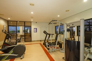 Uma academia com aparelhos de cardio, equipamentos de musculação e um espelho grande.