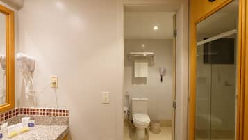 Casa de banho com secador de cabelo no balcão, sanita e cabine de duche com porta em vidro.