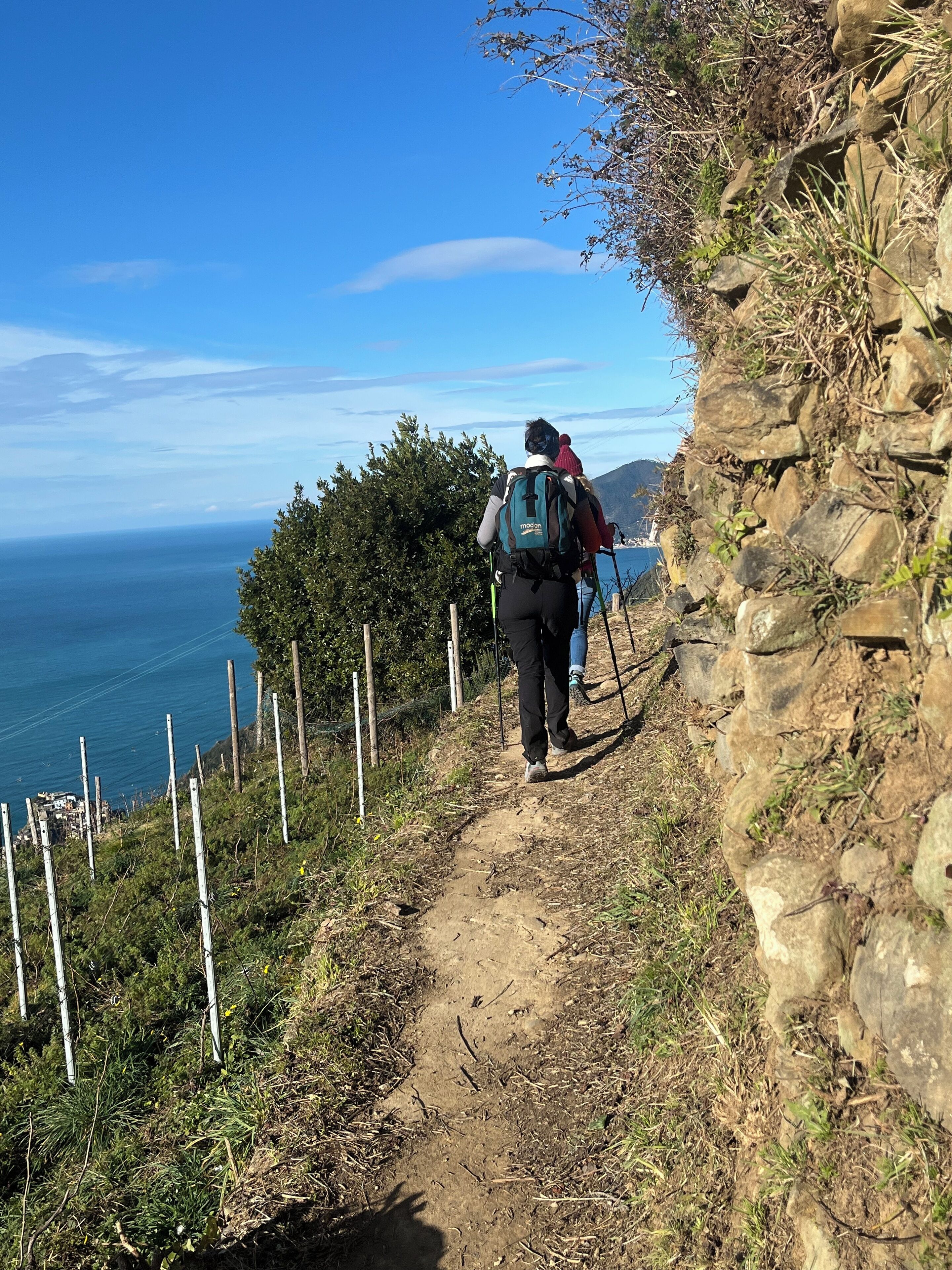 Uma trilha para caminhada com um caminho pedregoso, uma cerca de madeira e vista para o oceano.