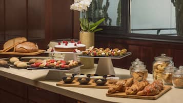 Buffet com diversos pastéis, sobremesas e pães em um balcão.