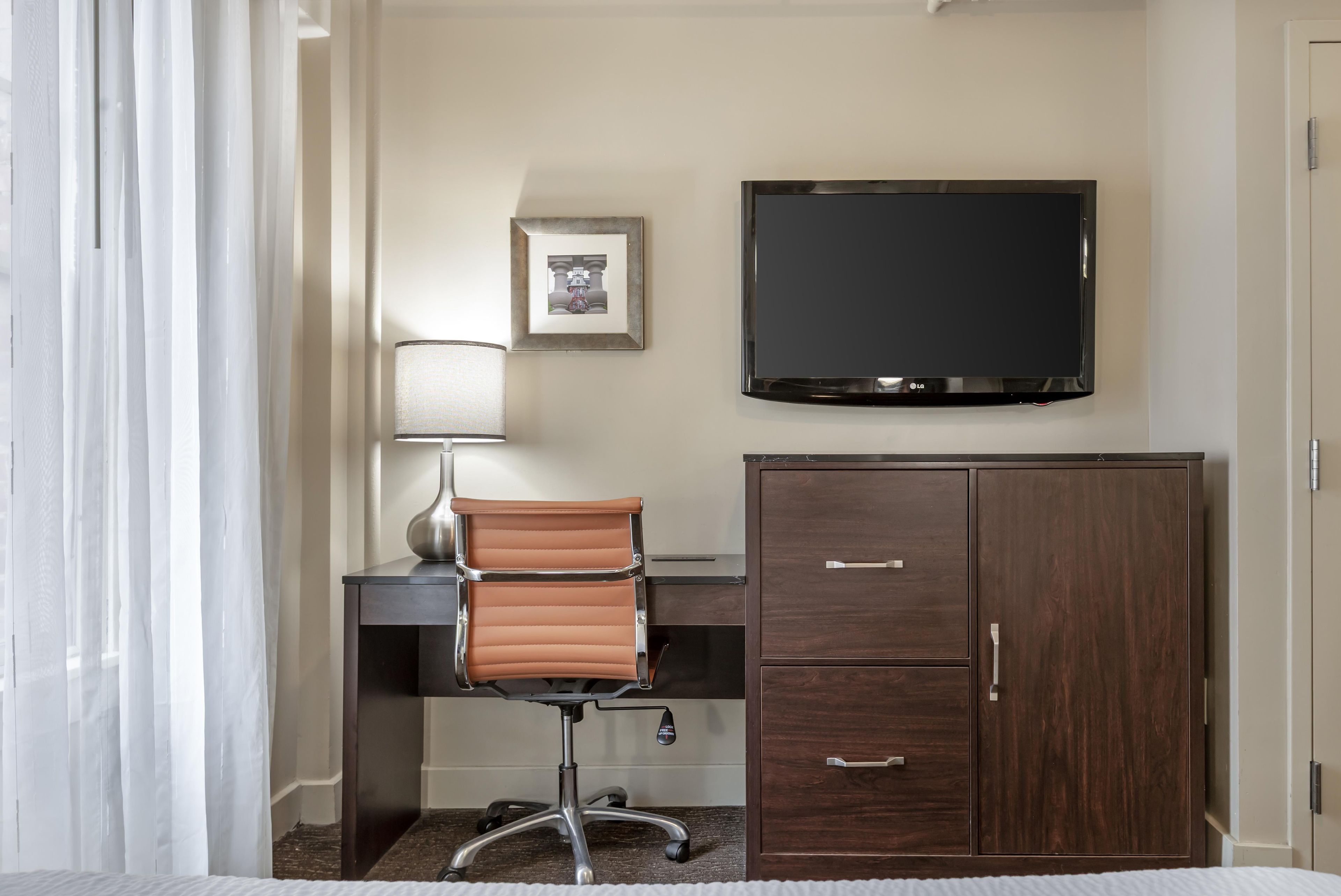 Quarto de hotel com escrivaninha, cadeira, televisão e guarda-roupa.