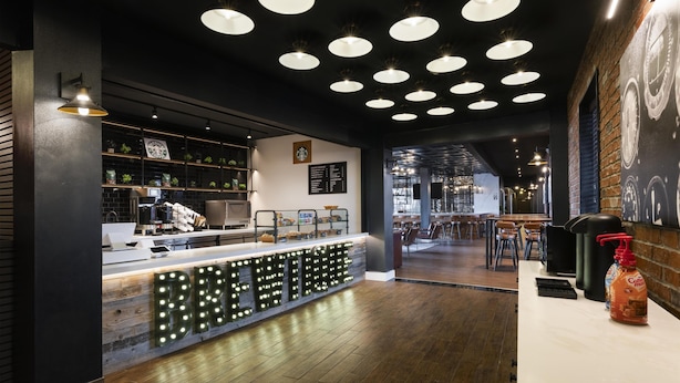 Interior moderno de café com balcão, prateleiras com plantas e área de estar.