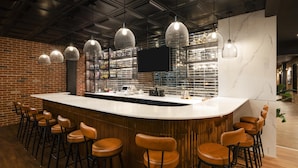 Uma área de bar com balcão curvo, vários bancos, iluminação pendente, uma televisão de tela plana e uma parede de tijolos.
