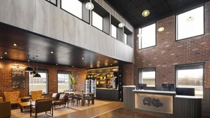 Um hall amplo com teto alto, paredes de tijolos aparentes, um balcão de recepção e uma área de estar com poltronas e mesas de couro.