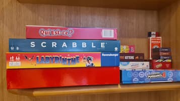 Uma prateleira com vários jogos de tabuleiro, incluindo Scrabble, Labyrinth, Ravensburger e Qui Est-ce?