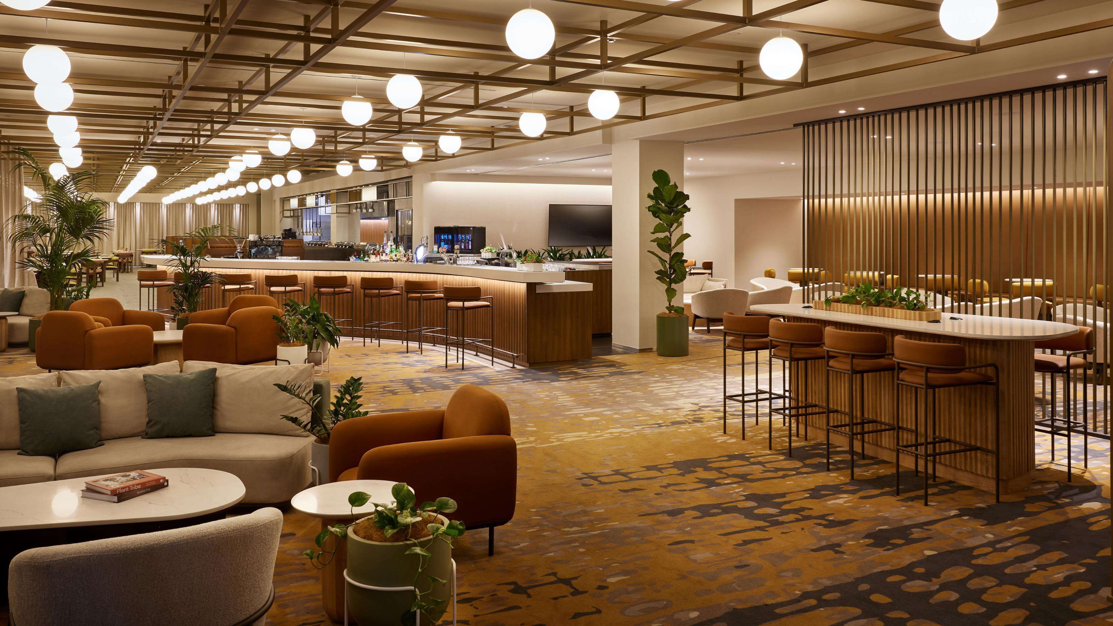 Um hall de hotel moderno com área de bar, sofás e uma tela grande.