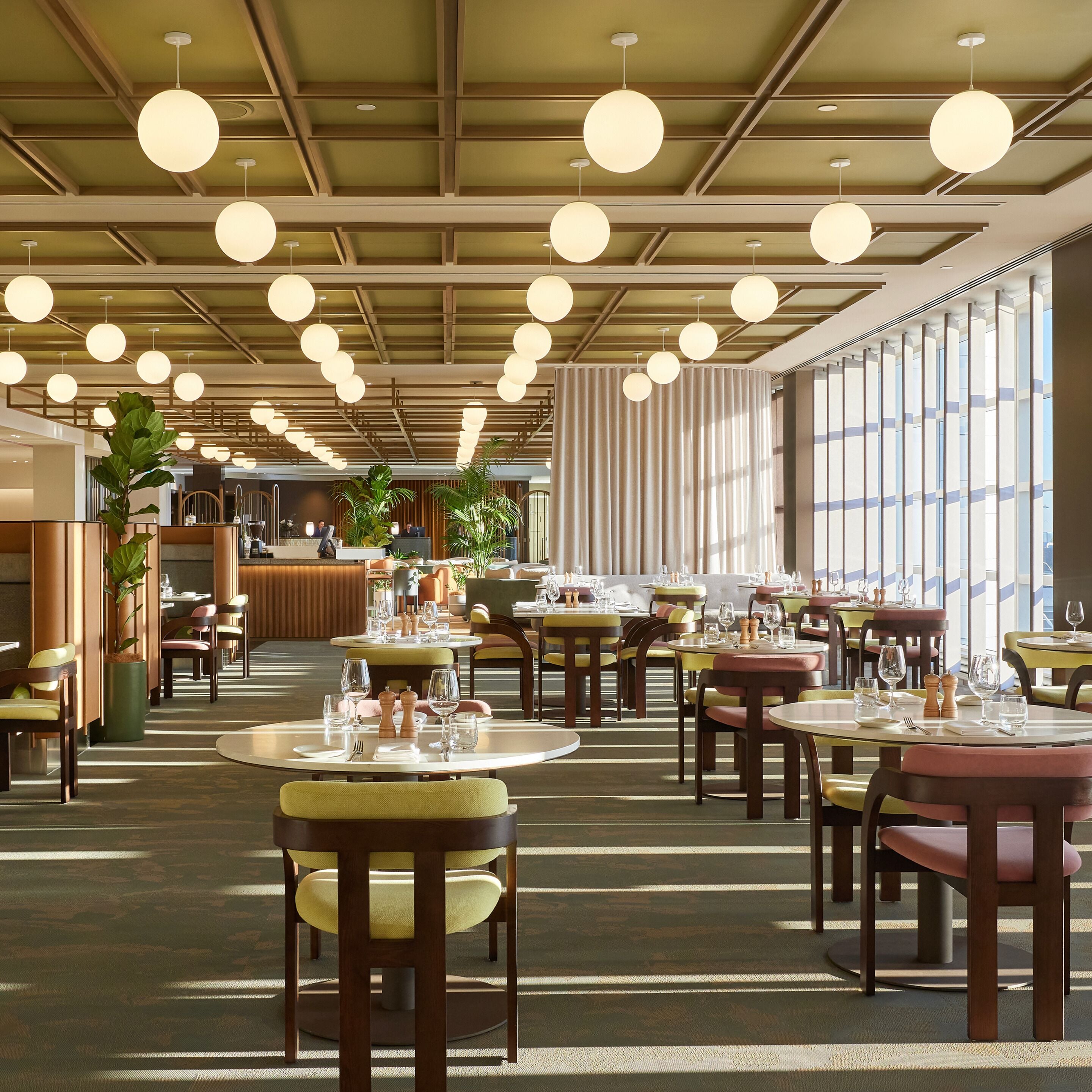 Um restaurante amplo com mesas redondas, cadeiras e luminárias esféricas penduradas.
