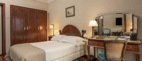 Quarto de hotel com cama, escrivaninha, cadeira, guarda-roupa e espelho.