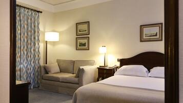 Quarto de hotel com cama, sofá, mesa de cabeceira, luminária e duas quadros na parede.