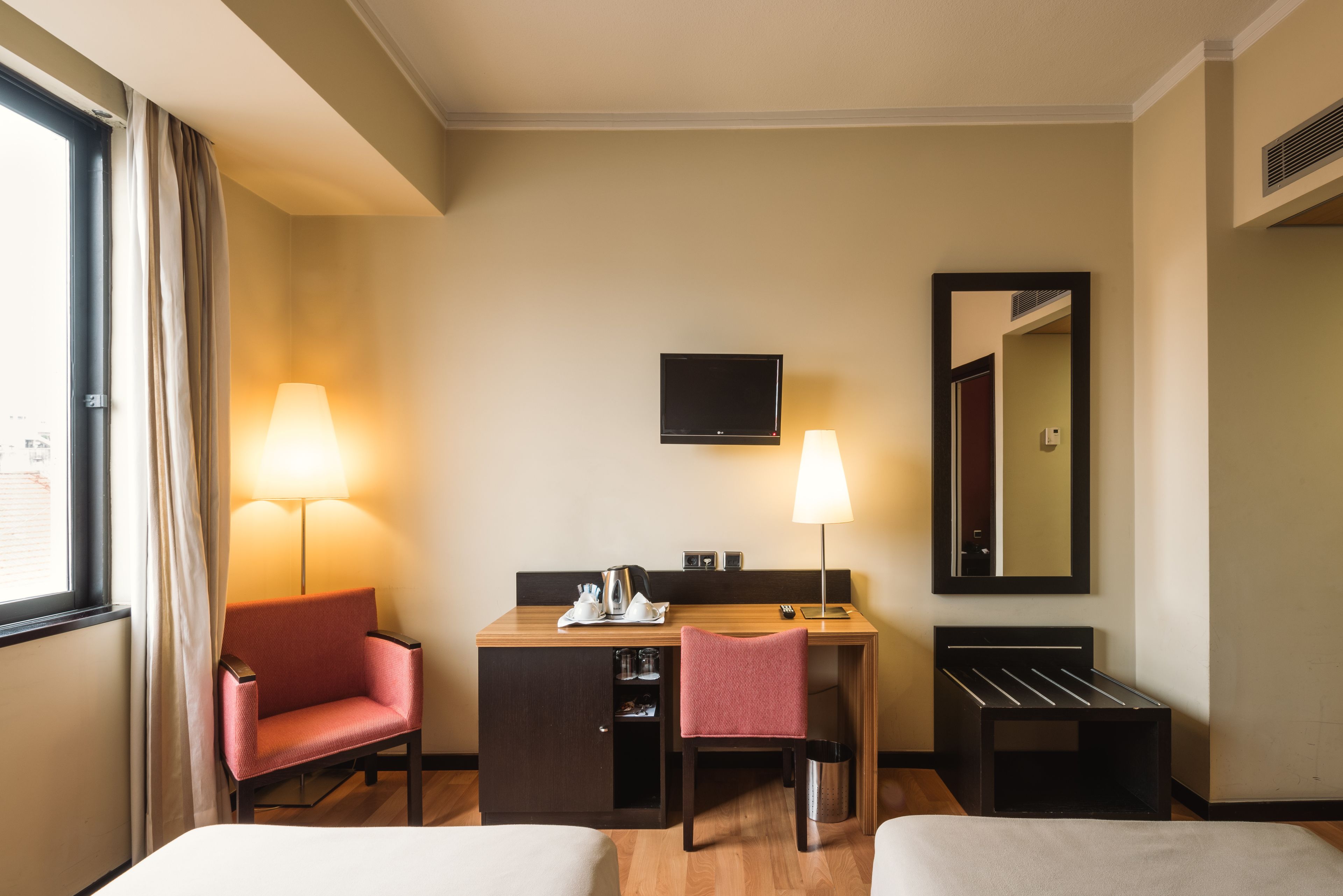 Quarto de hotel com cama, escrivaninha com cadeira, televisão e espelho.
