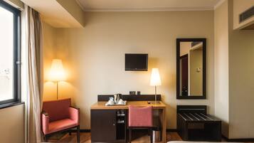 Quarto de hotel com cama, escrivaninha com cadeira, televisão e espelho.