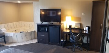Quarto de hotel com uma banheira grande, uma escrivaninha com computador, uma cadeira e uma televisão.