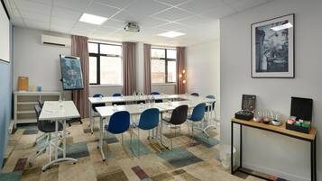 Uma sala de conferências com uma mesa comprida, cadeiras, um projetor e um quadro na parede.