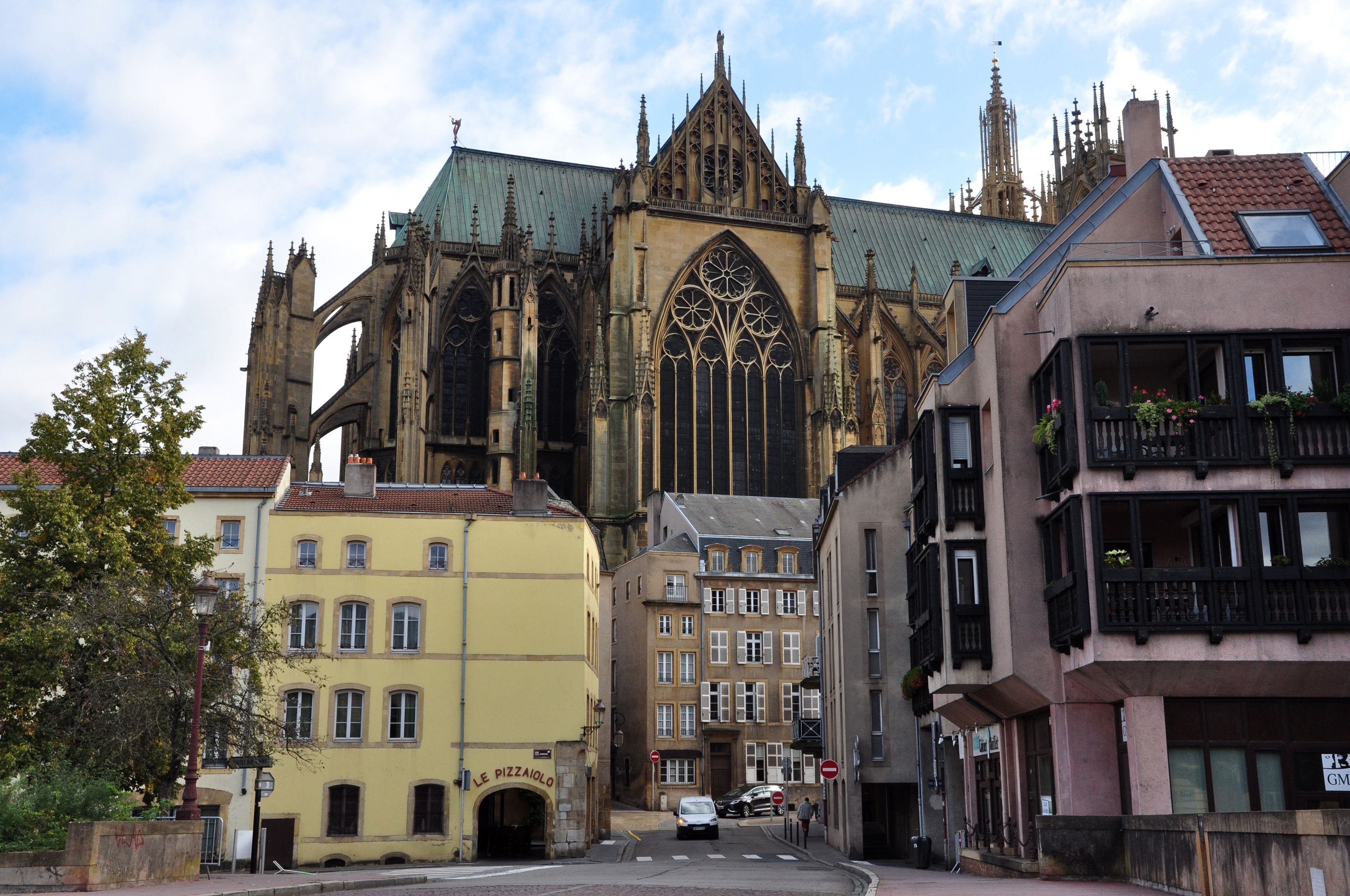 Uma catedral histórica com arquitetura gótica, uma rua em frente com edifícios, e um céu claro.