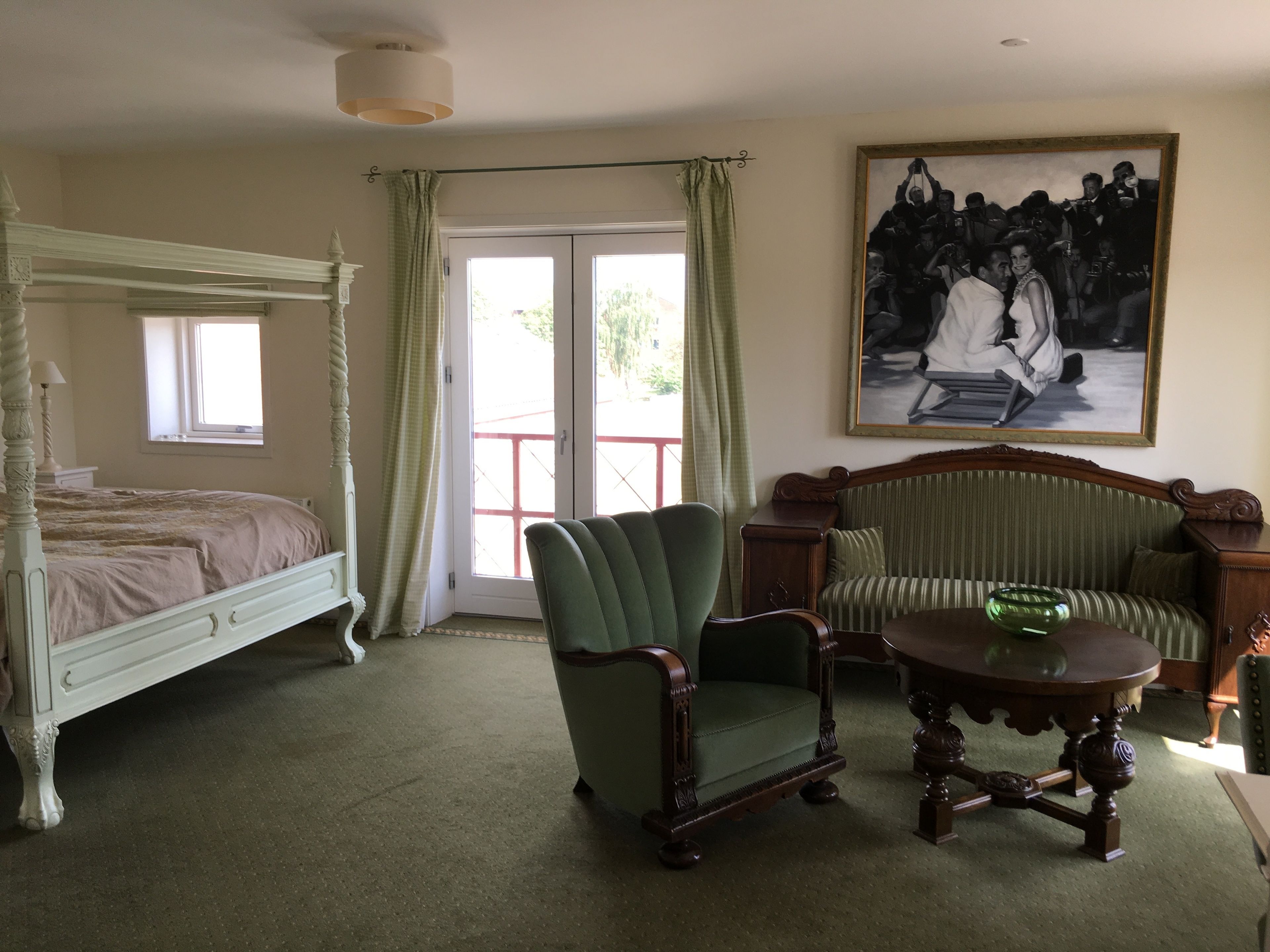 Quarto com cama de dossel, uma poltrona verde, um sofá listrado e um quadro na parede.